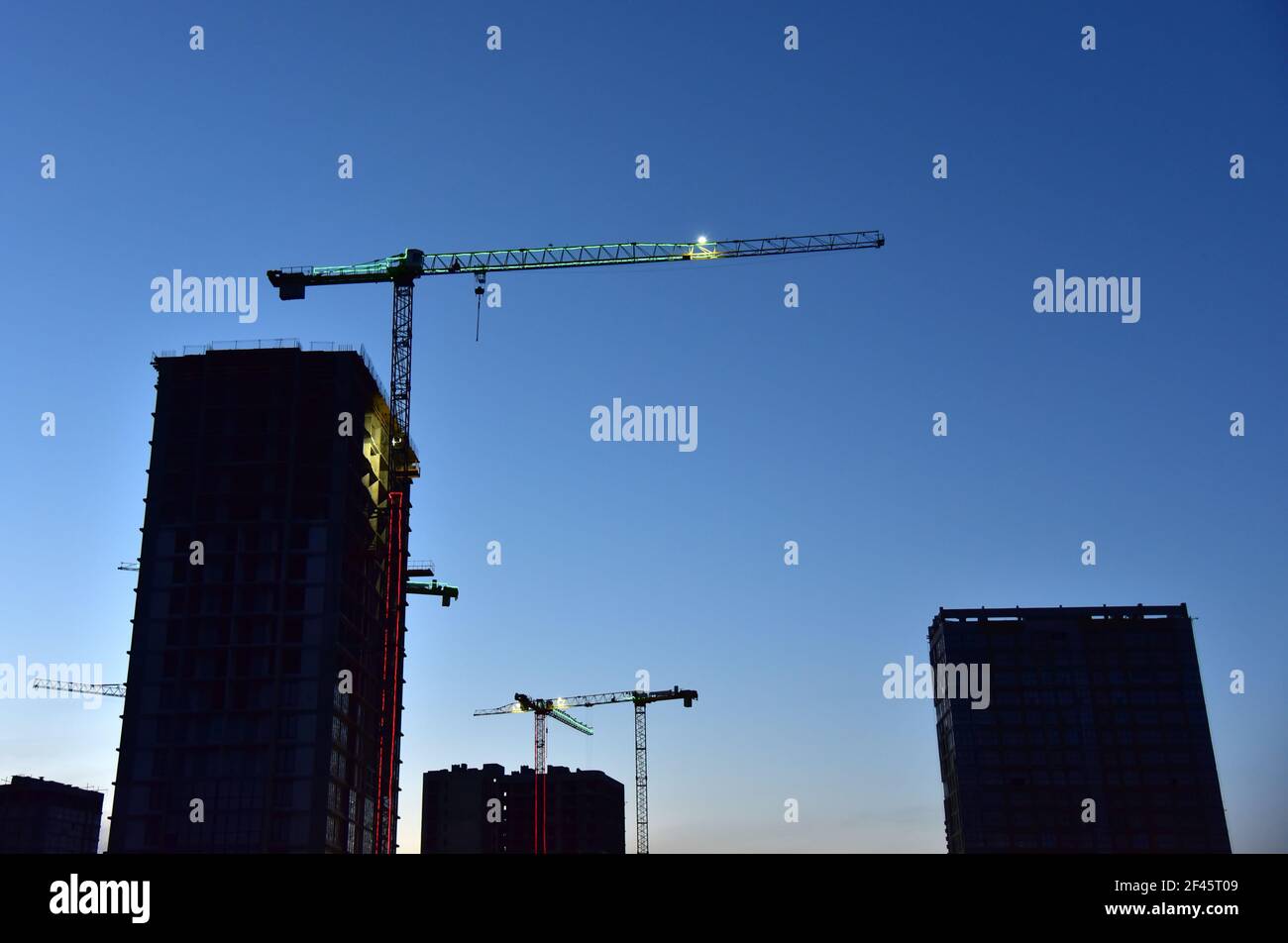 Tower cranes in action at construction site on sunset background. Crane ...
