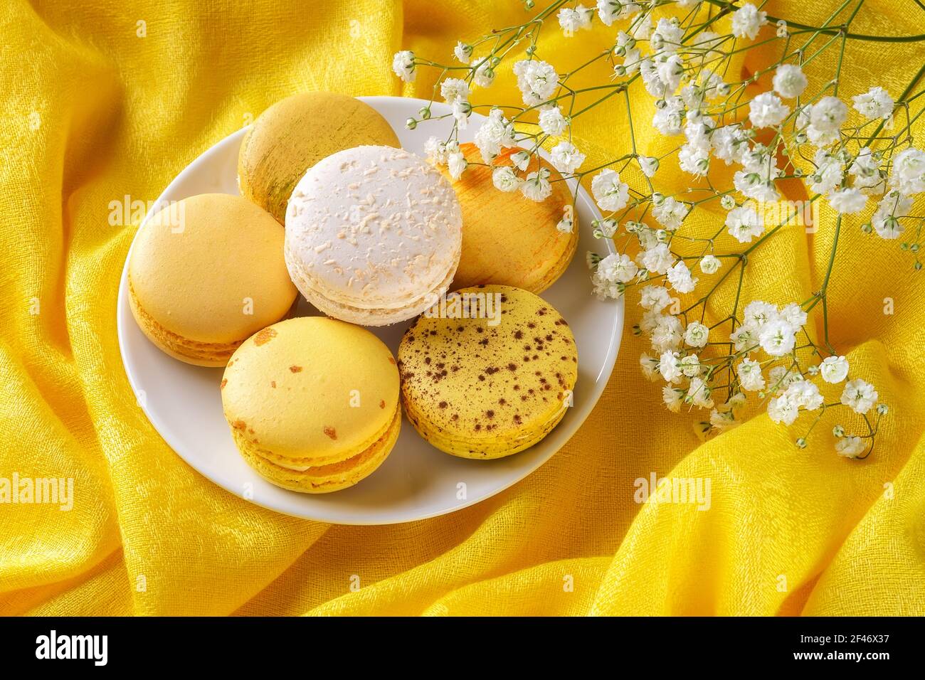Yellow macaroons on a white elegant saucer against bright yellow draped ...