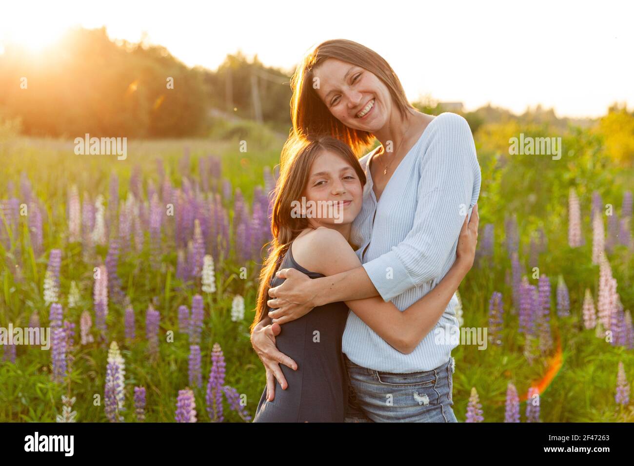 Young mother embracing her child outdoor. Woman and teenage girl on summer field with blooming ...
