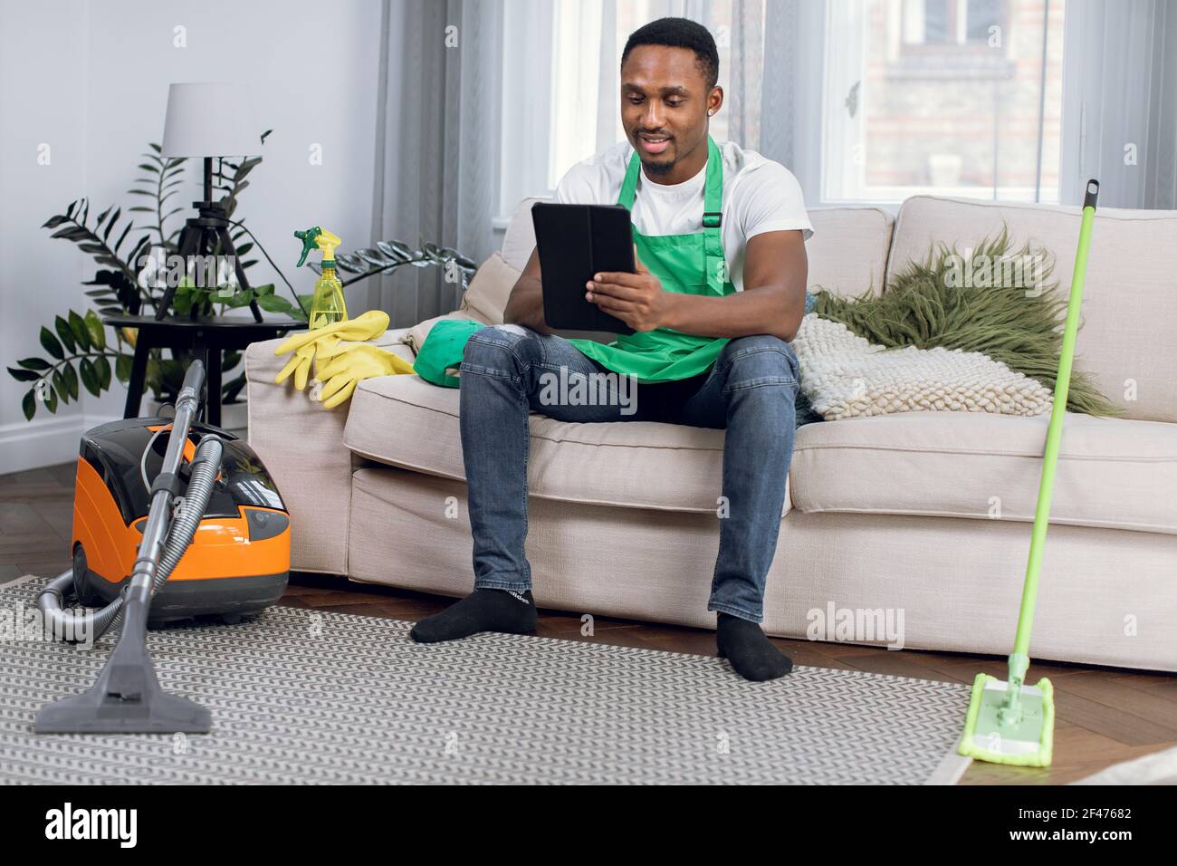 African cleaner using digital tablet while relaxing on couch Stock ...