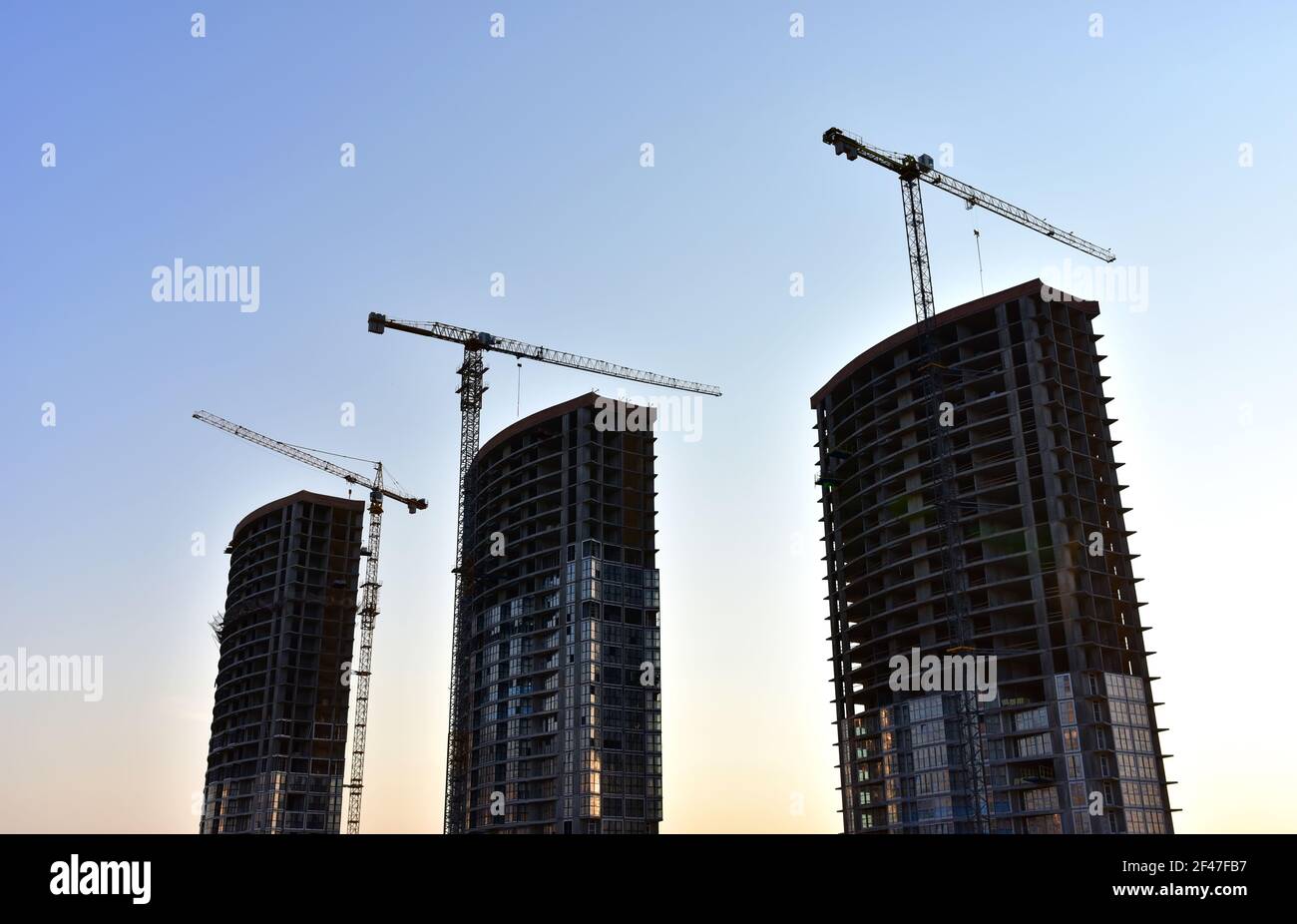 Tower cranes in action at construction site on blue sky background. A ...