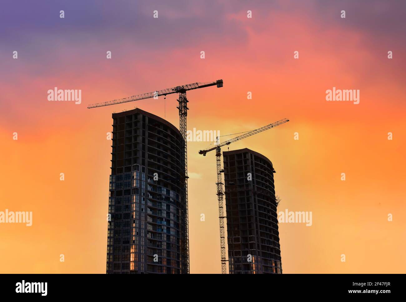 Tower cranes in action at construction site on sunset background. A ...