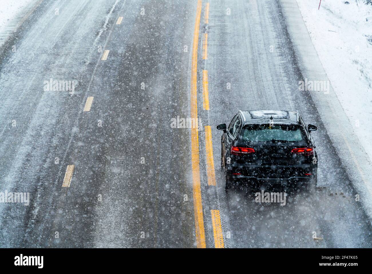 Car driving on a highway with wet slippery asphalt during a snow storm ...