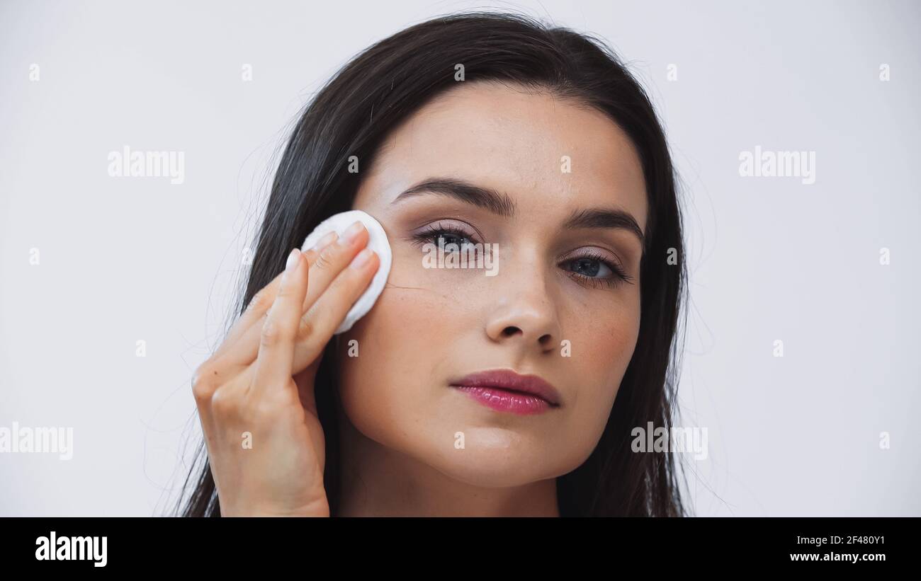 brunette woman wiping face with cotton pad while looking at camera ...