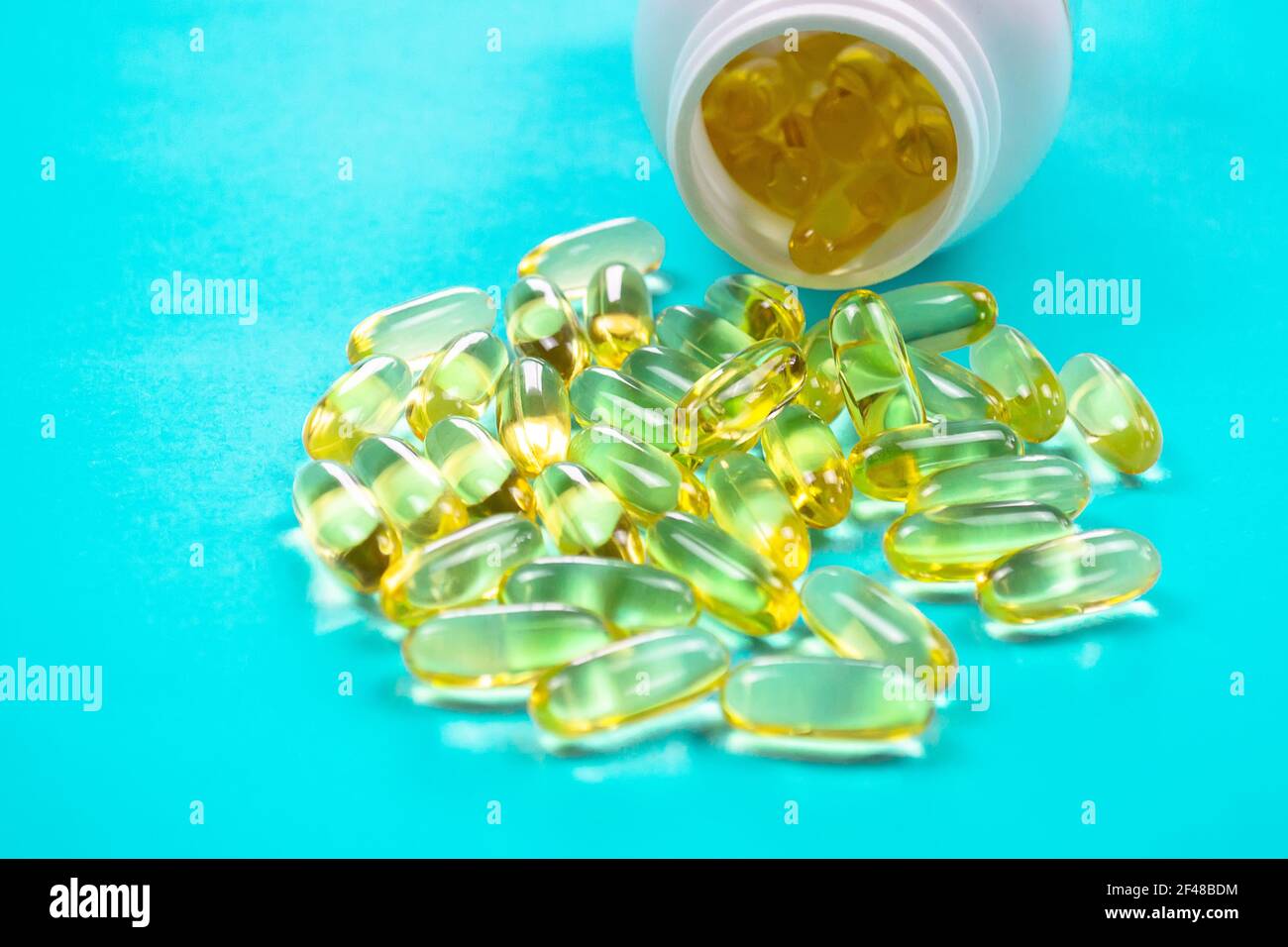 Omega 3 fish oil capsules spilling out of a bottle on a blue background ...