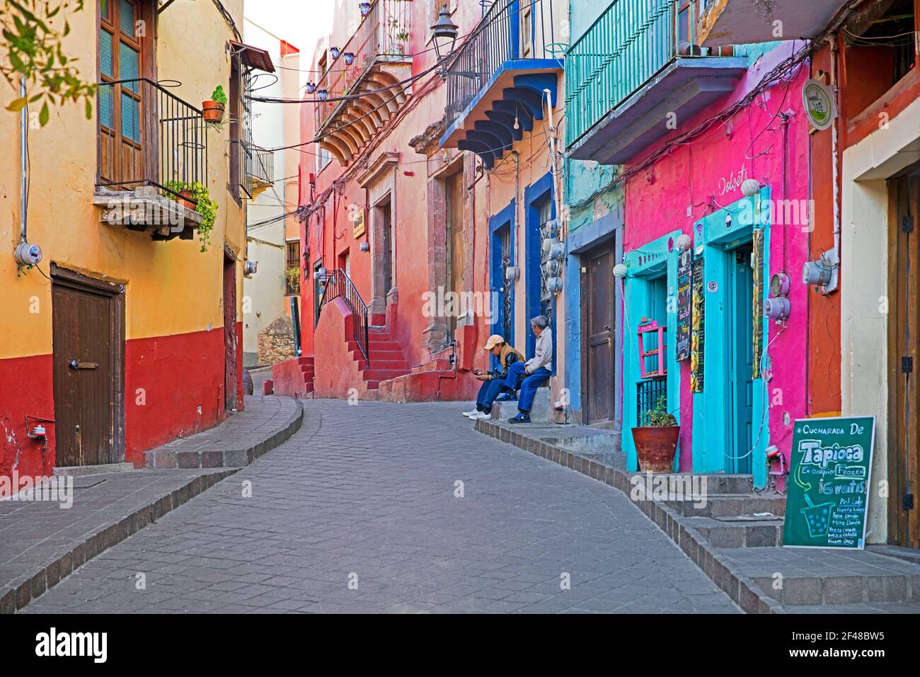 Colourful colonial era houses with balconies in alley paved with square ...