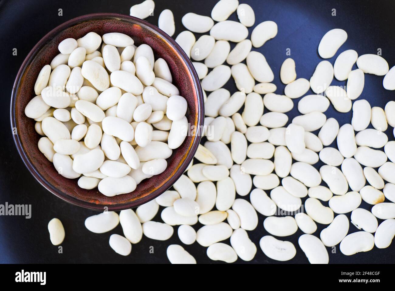 A top view of healthy white beans in the bowl and on the dark ...