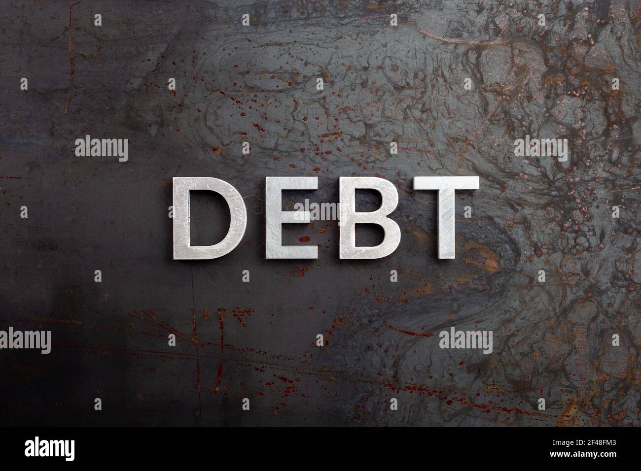 the word debt laid with silver letters on raw rusted steel sheet ...
