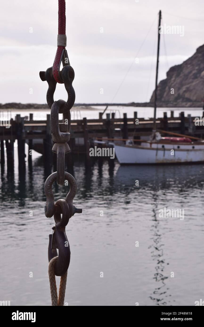 A Vertical shot of a long hanging metal chain link showing an old boat ...