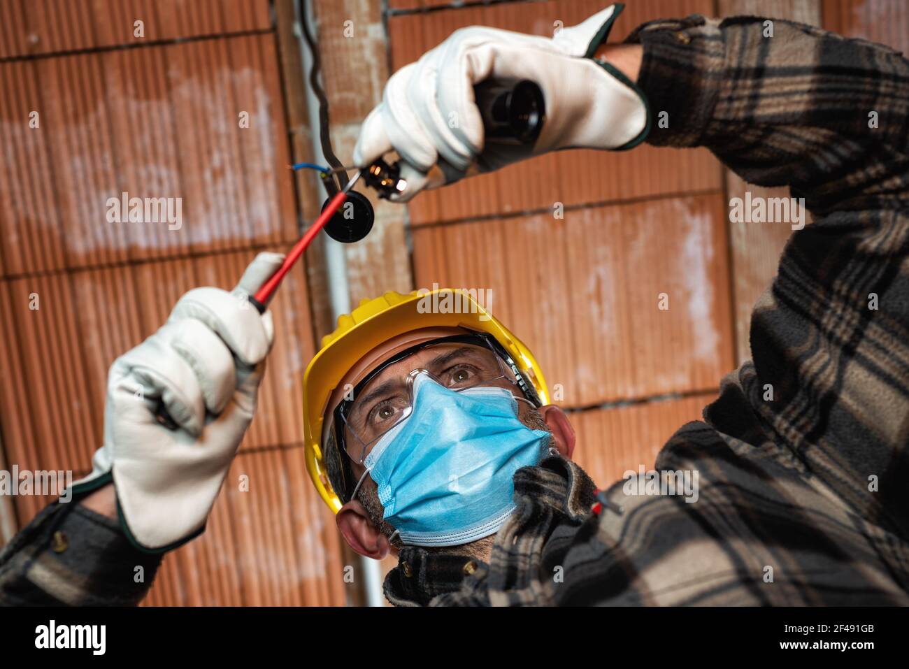 Electrician worker at work replaces the lamp holder protected by helmet ...