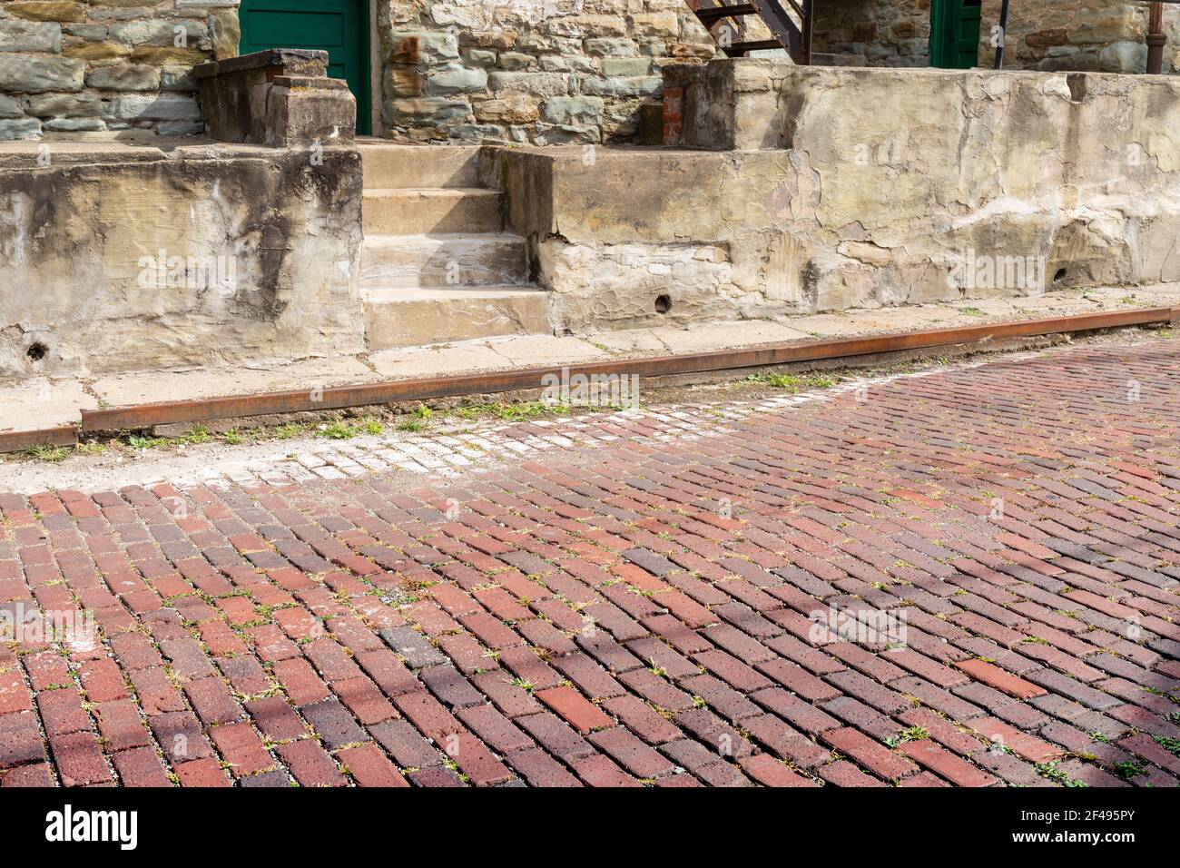 Brick street beside a narrow sidewalk, curb of rusted metal, crumbling ...
