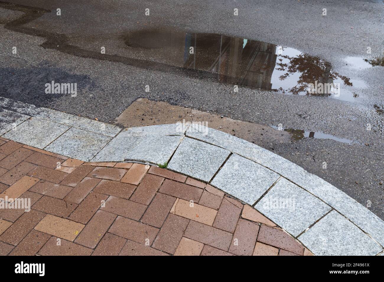 Reflections of sky and urban buildings in a street puddle bordered by a ...