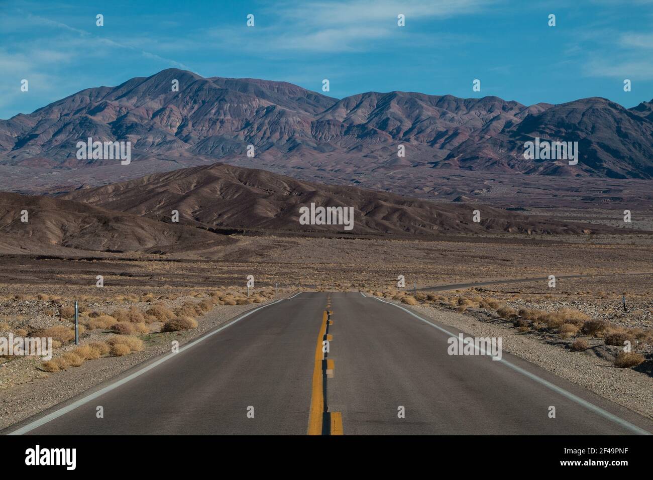 Wide shot of the road in the desert, with a mountain straight ahead ...