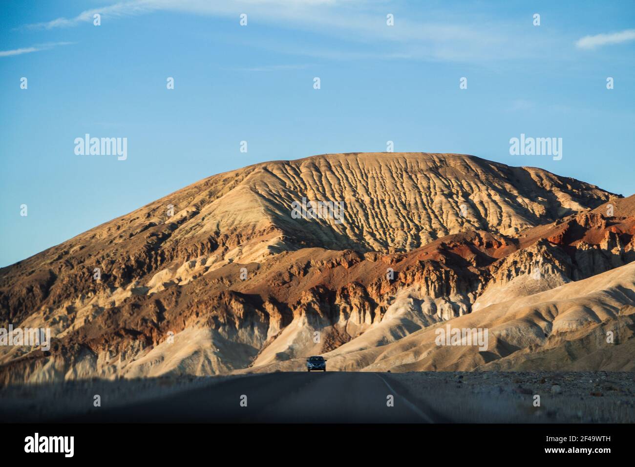 Red rock formations behind a car driving down the road in Death Valley ...