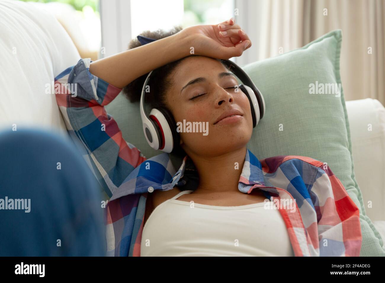 Mixed race woman lying on couch listening to music with headphones at ...