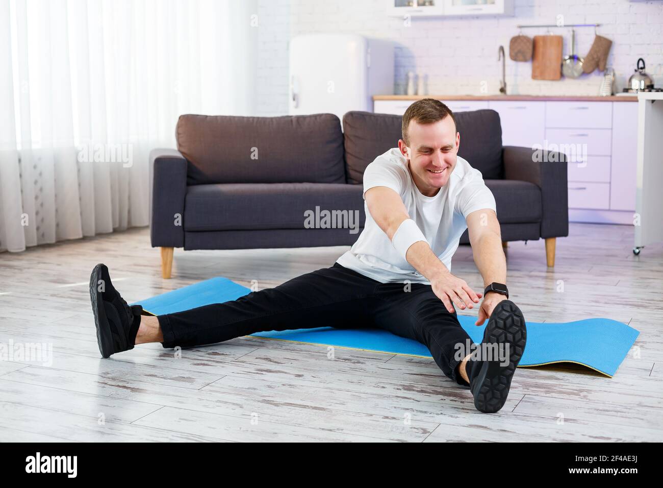 Muscular athletic man in a t-shirt doing warm-up exercises at home ...
