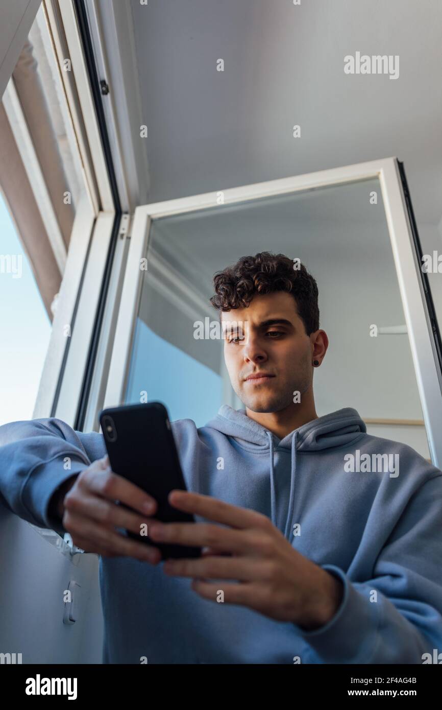 A low angle shot of a young Caucasian male using his smartphone leaning ...