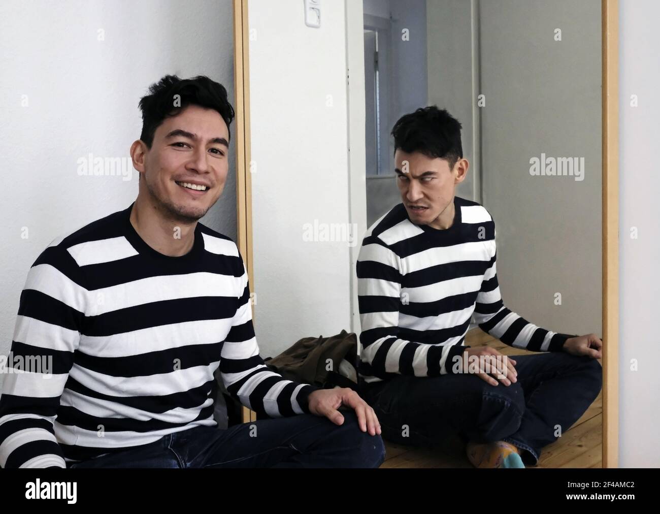 A Caucasian smiling man sitting in front of a mirror while his alter ...