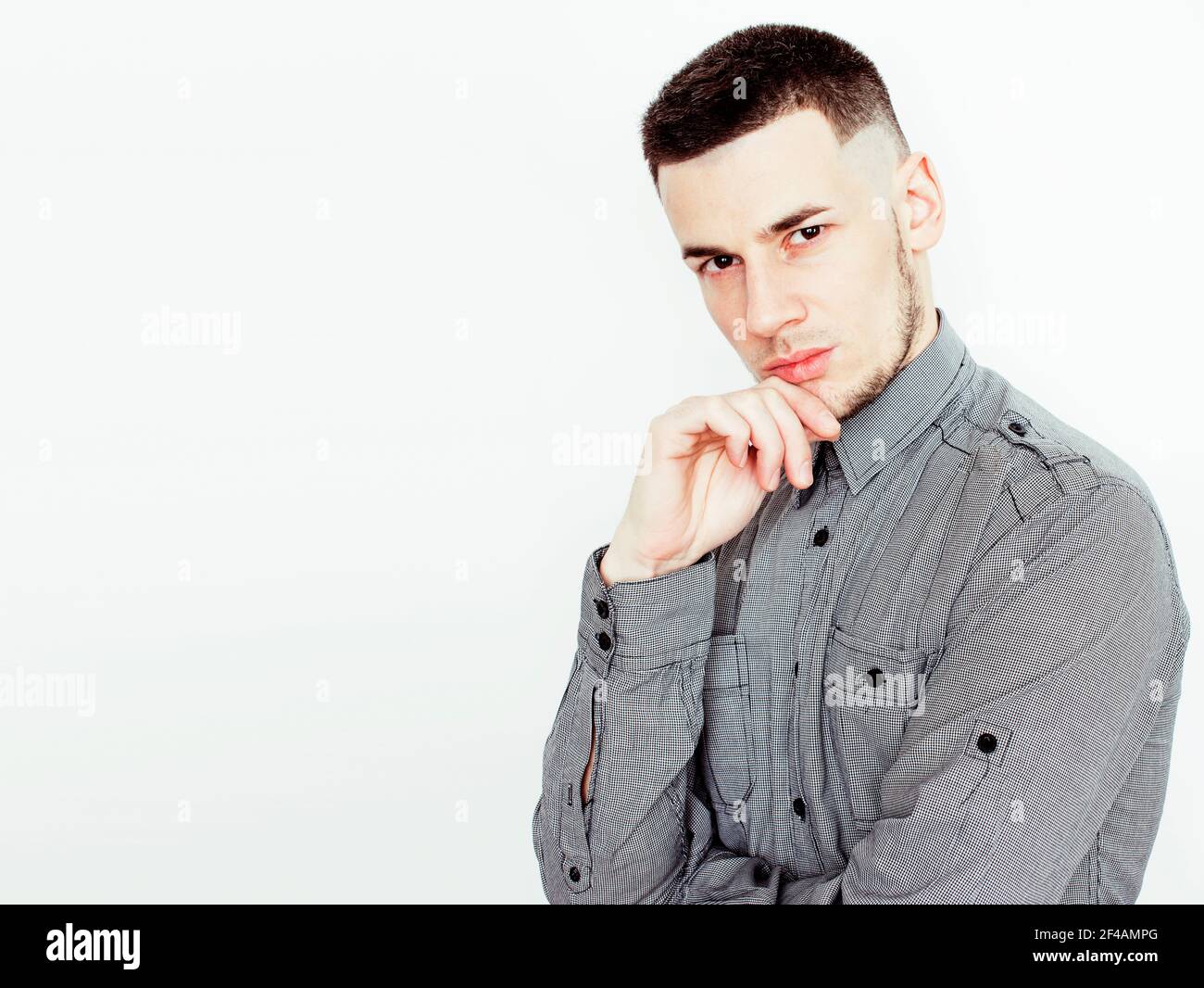 Portrait of a smart serious young man standing against white background ...