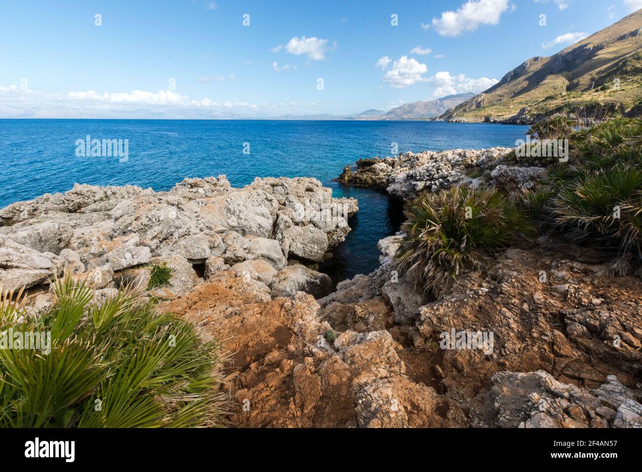 A landscape of rocks and hills surrounded by the sea under a blue sky ...