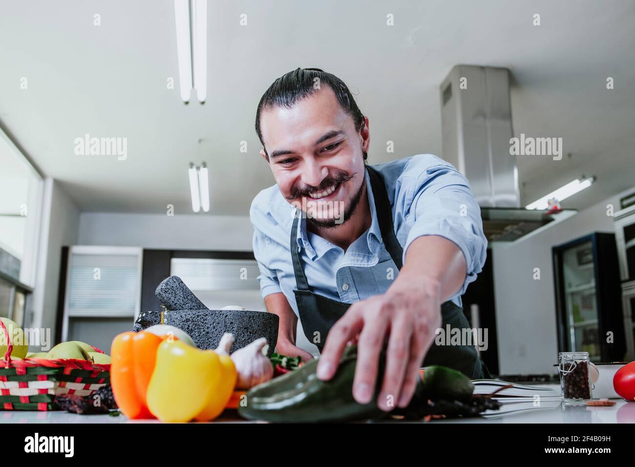 latin man cooking at home preparing salad or mexican sauce in kitchen ...