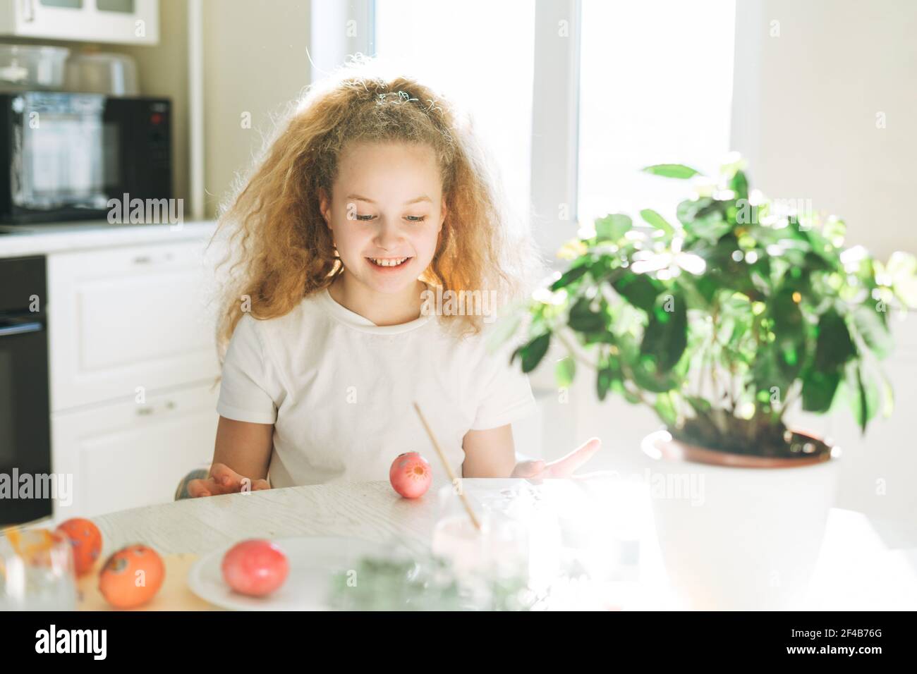 Cute tween girl with long curly hair painting eggs on kitchen at home ...