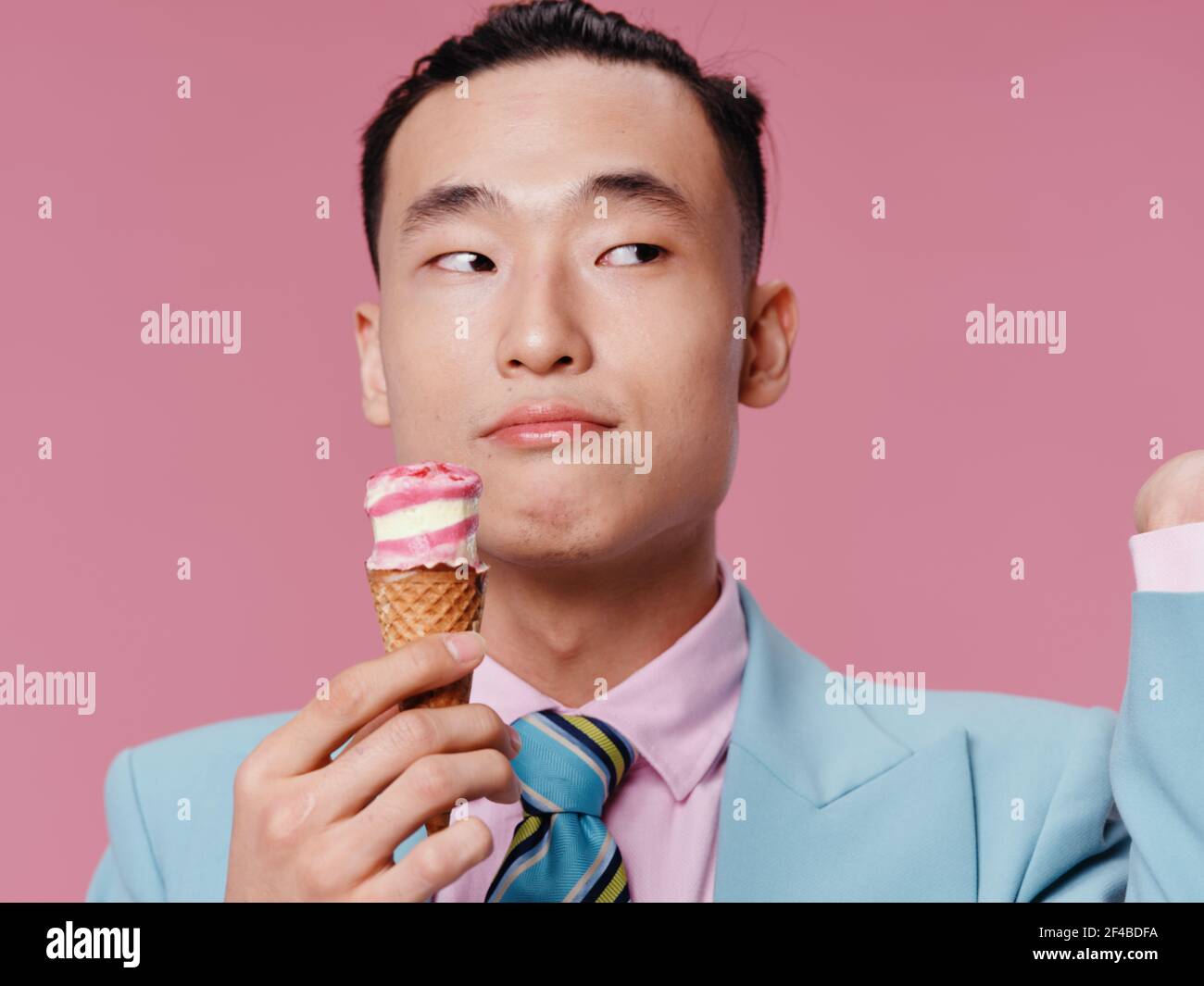 Happy asian man eating ice cream on pink background in blue classic ...