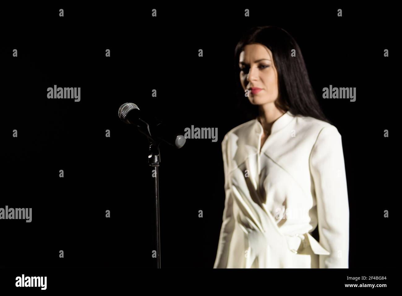 Portret of a singer with mic singing popular song on stage in white ...