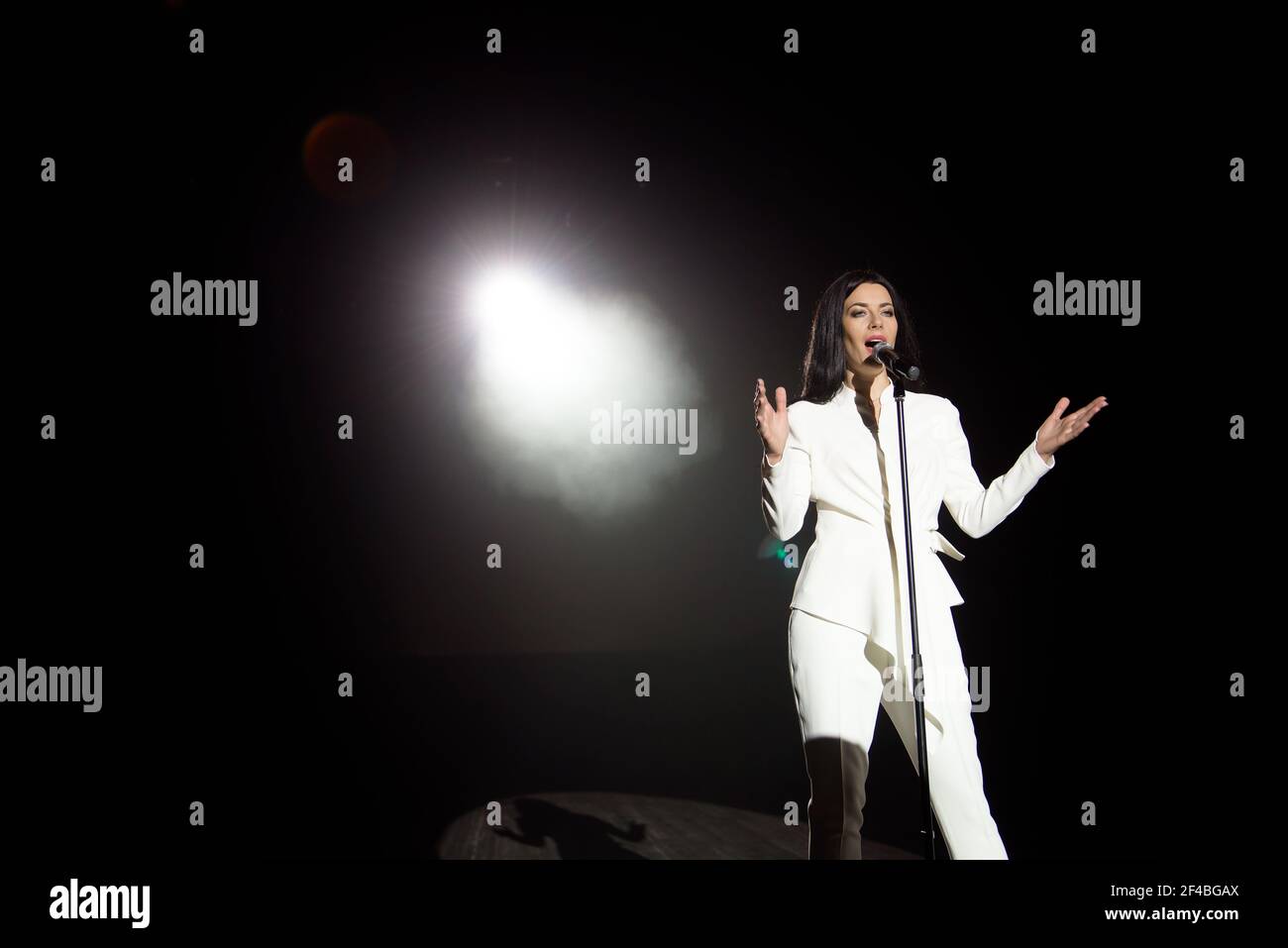 Singer woman on stage with black background in a beam of white light ...