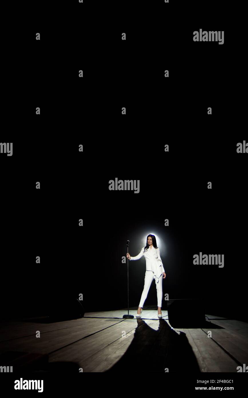 Singer woman on stage with black background in a beam of white light ...