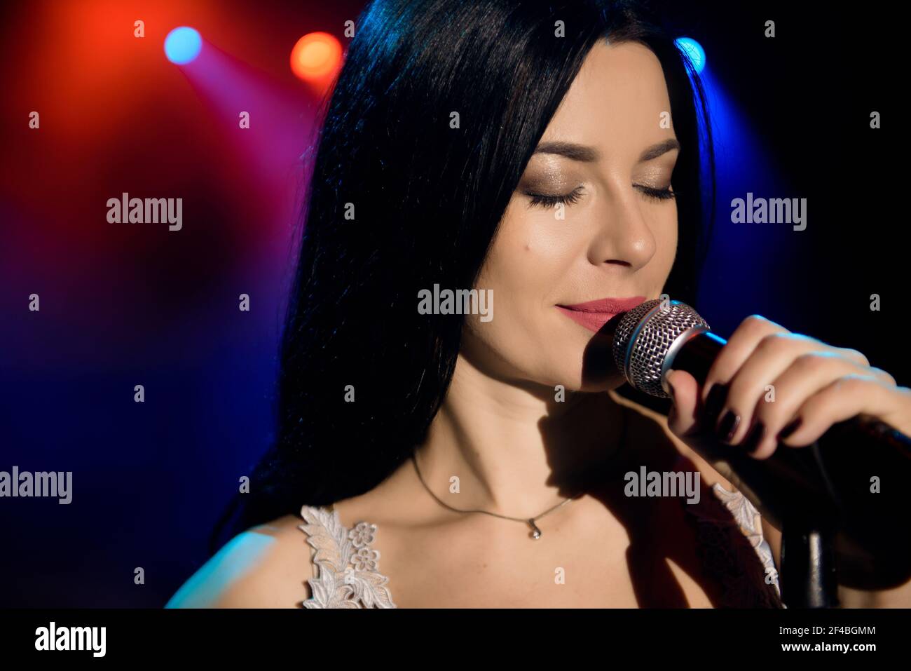 A female singer holding microphone against the colorful lights of the ...