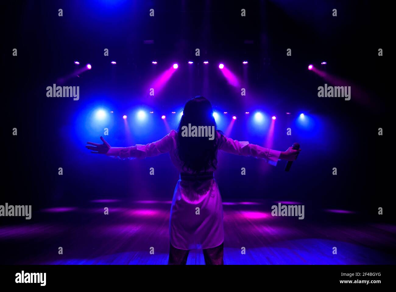 Unrecognizable singer standing on stage at microphone, back view, neon ...