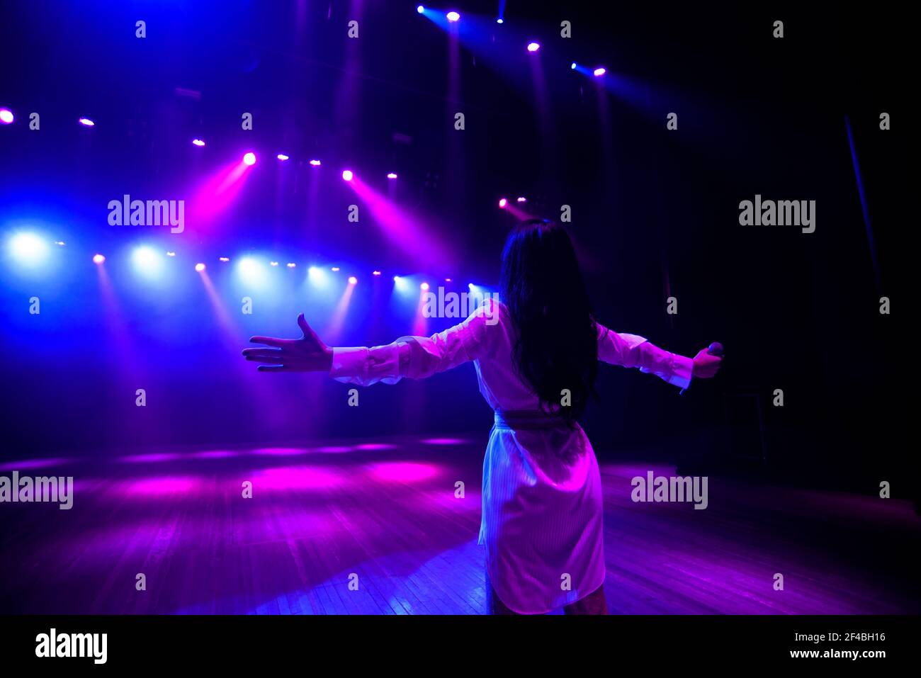 Unrecognizable singer standing on stage at microphone, back view, neon ...