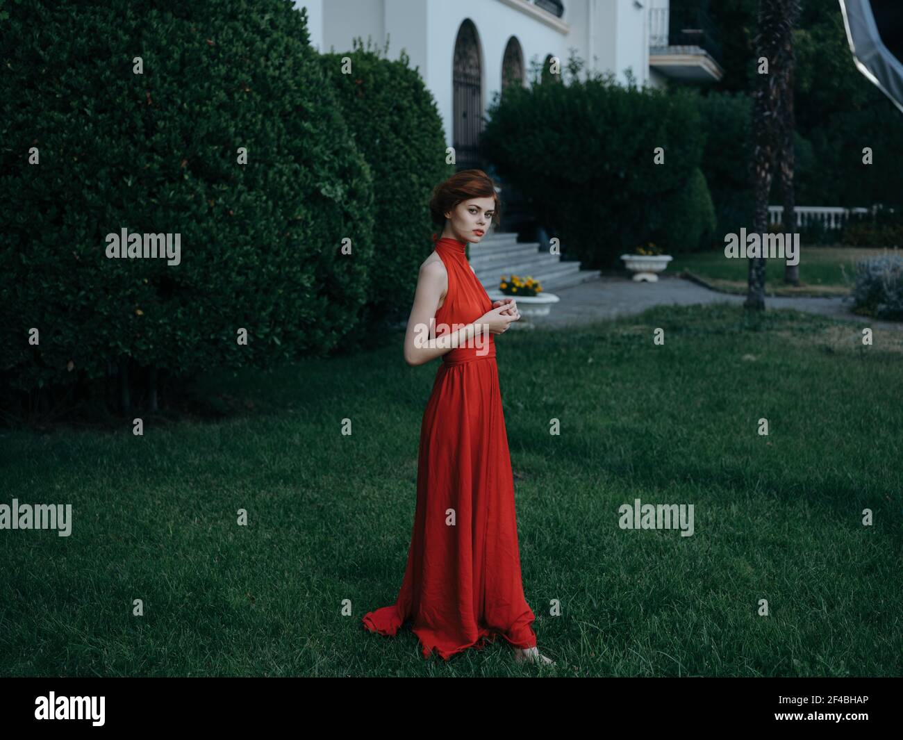 Pretty woman in red dress nature green bush masquerade decoration walk ...