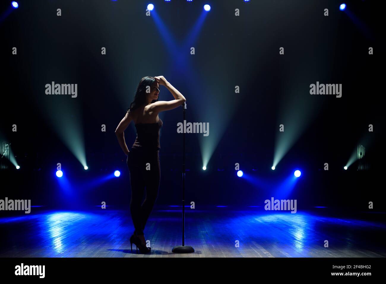 Silhouette of singer standing on stage at microphone in night club ...