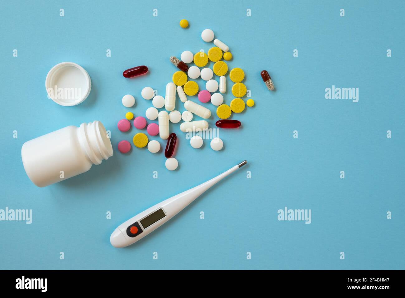 Multi-colored tablets, pills, capsules and digital thermometer on a ...