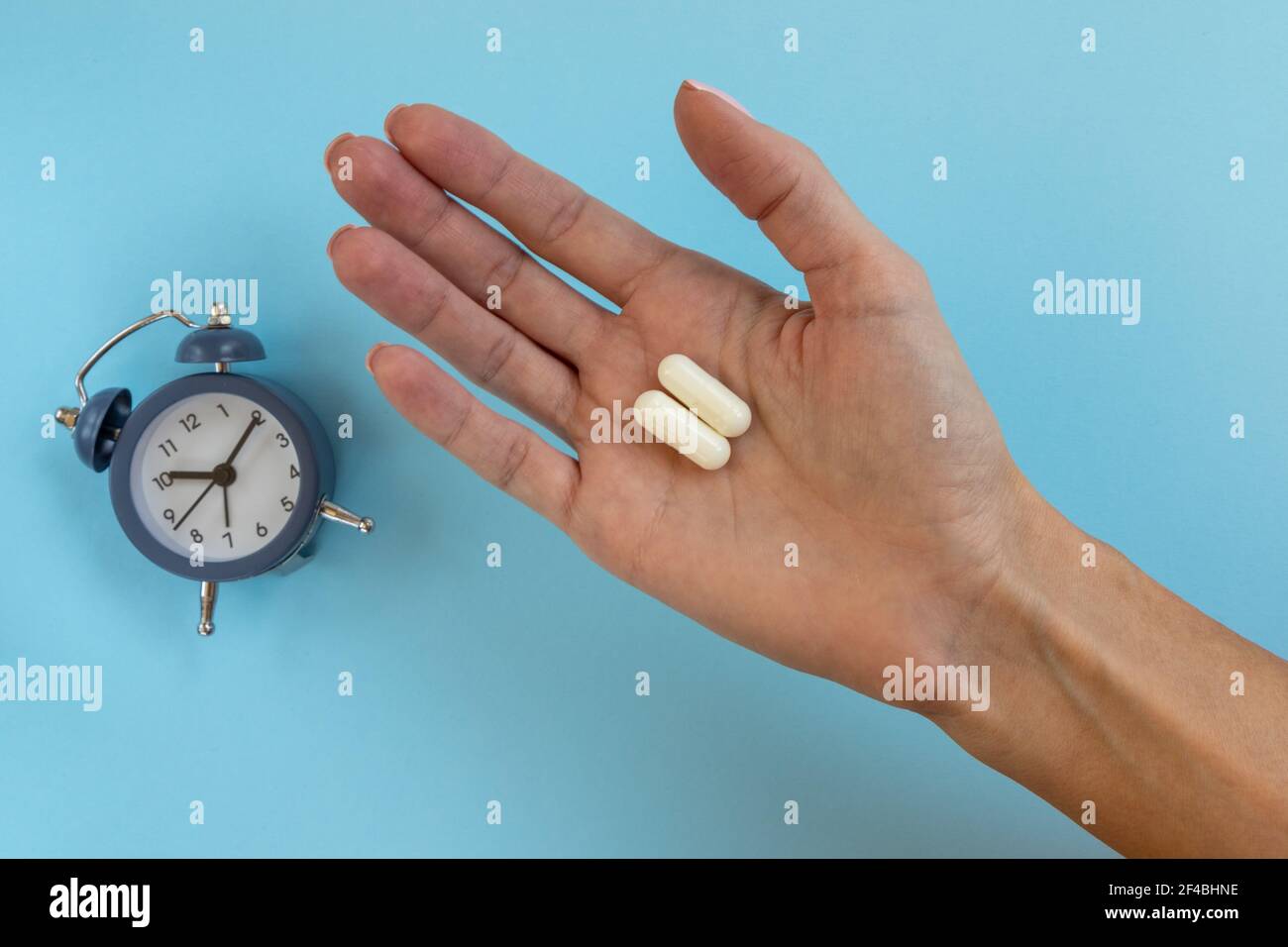 White capsule pill in women hand on alarm clock background. Female hand ...