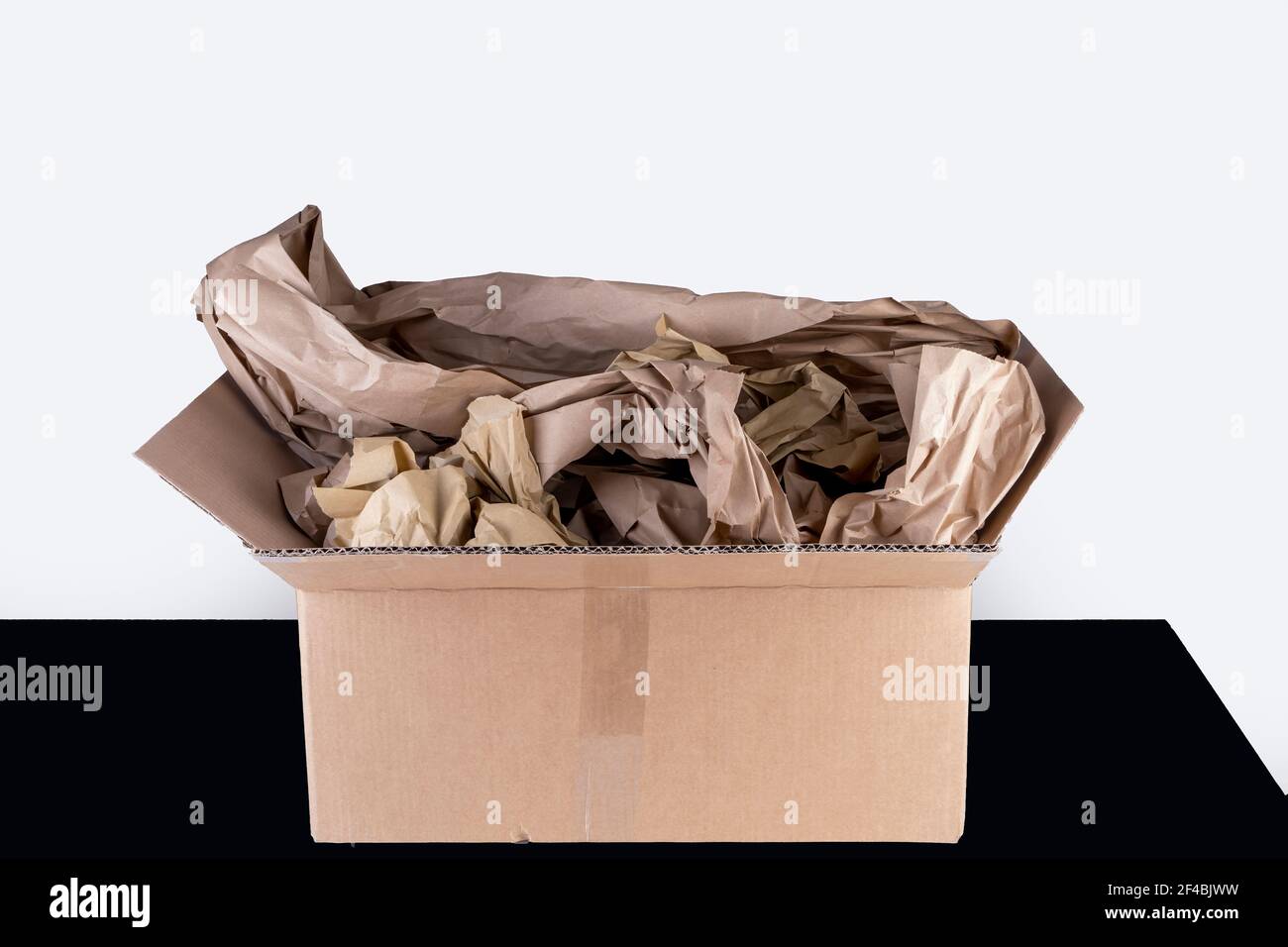 Open cardboard box on a black table, with paper filling. For safe ...