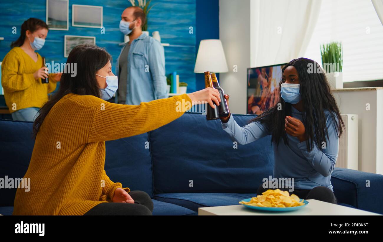 Mixed race black woman taking off protection masks clinking bottles of ...