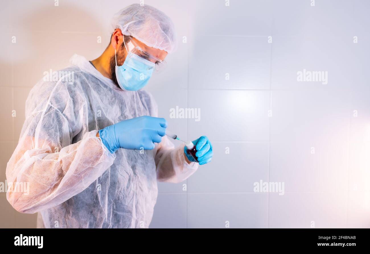 A male doctor in a protective suit preparing a syringe for vaccination ...