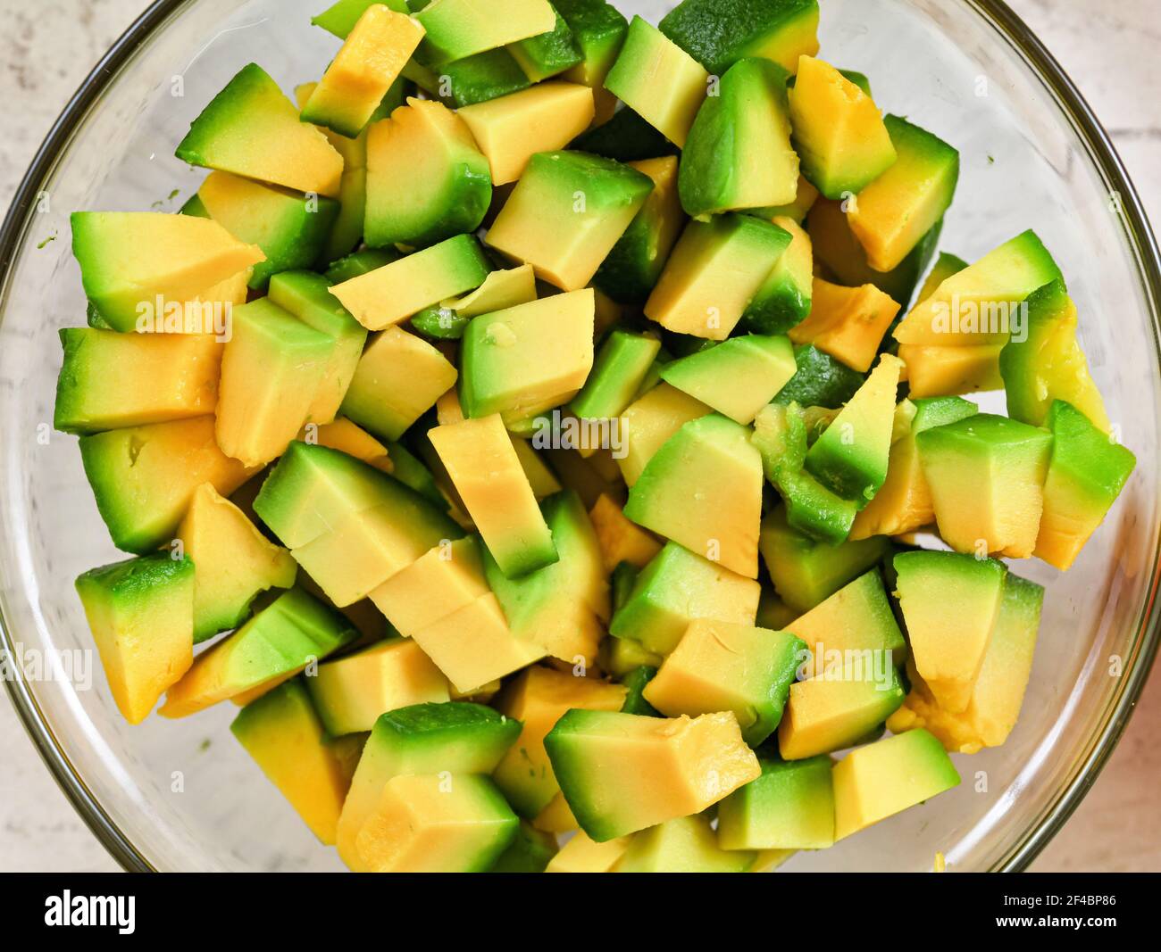 Yellow green avocado pulp cut to small pieces in glass bowl, view from ...