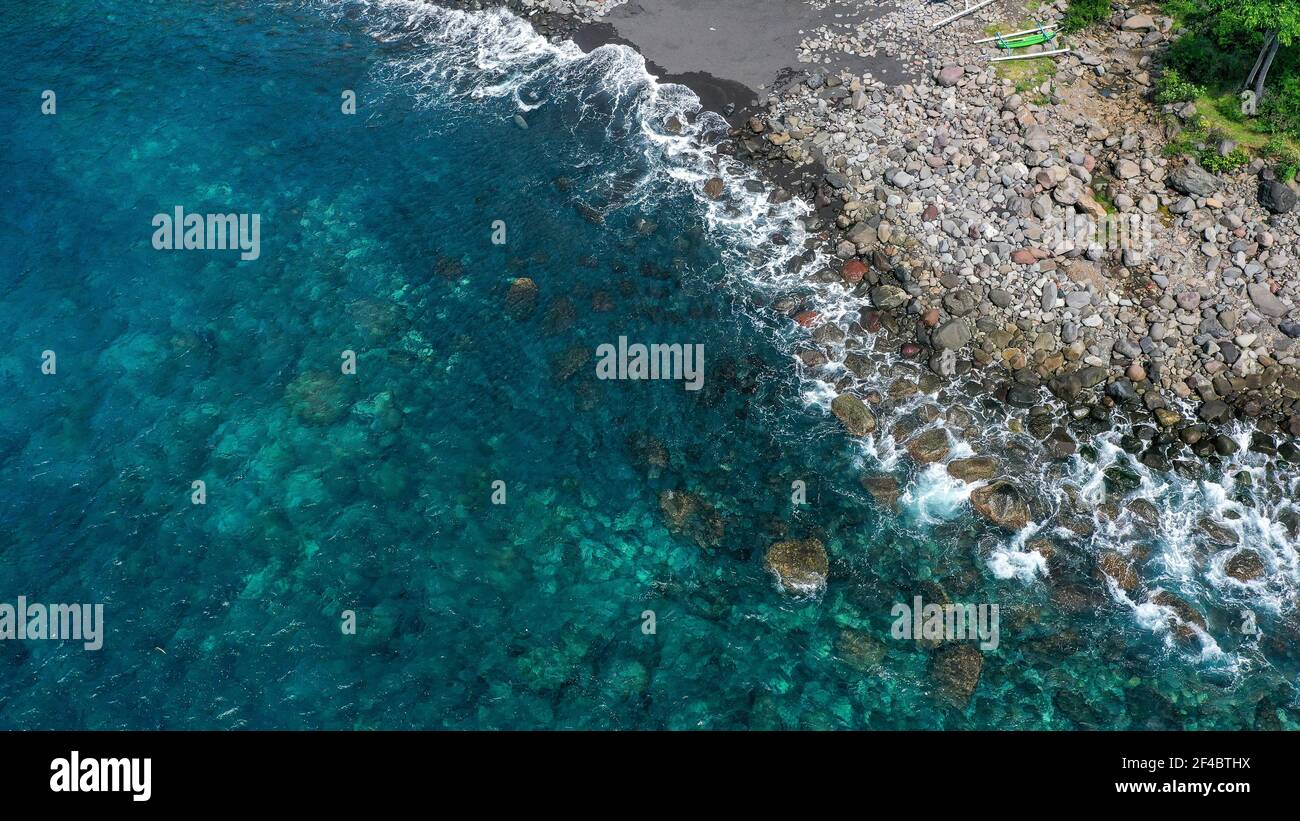 Aerial top view waves break on dark rocks near beach. Sea waves on the ...