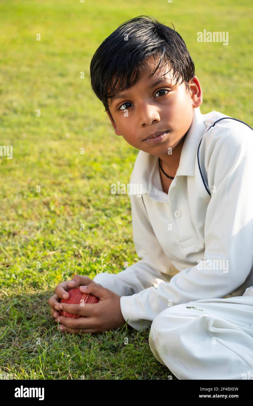 a boy sitting on the ground holding cricket ball Stock Photo - Alamy