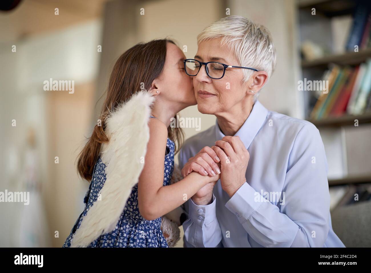Happy Granddaughter Kissing Grandmother In The Cheek At Home Stock