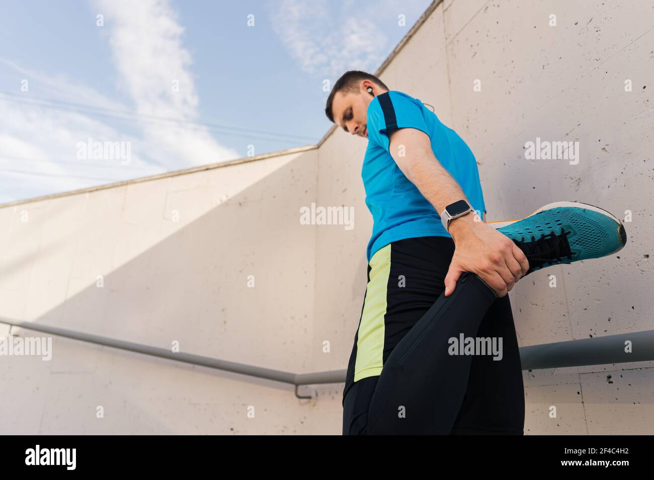 Young man runner getting ready to run stretching legs warm up quad ...