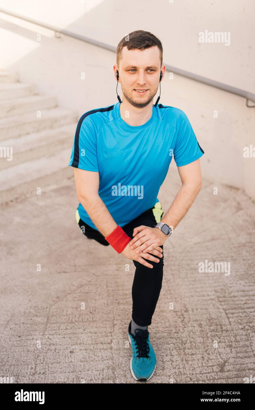 Young man runner getting ready to run stretching legs warm up quad ...