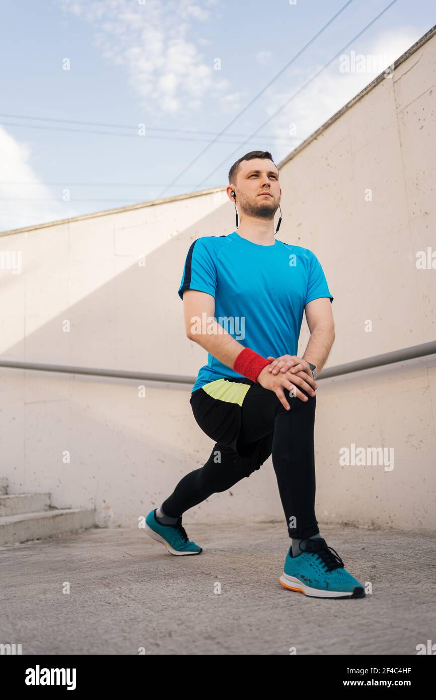 Young man runner getting ready to run stretching legs warm up quad ...