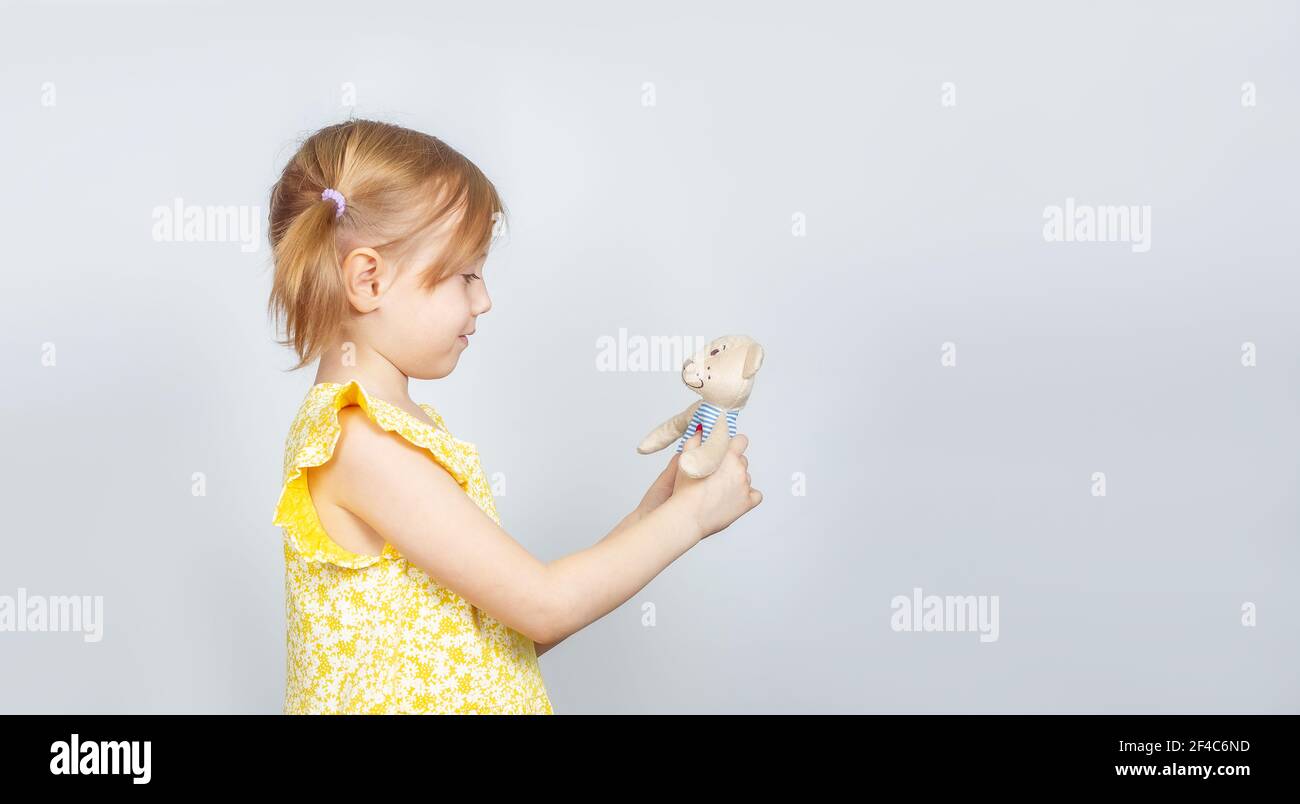 Little Caucasian girl with teddy bear standing sideways to the camera ...