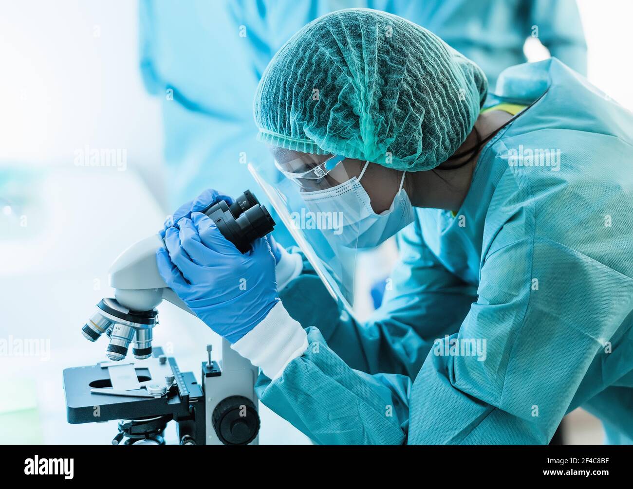 Female scientist examining coronavirus through microscope in hospital ...