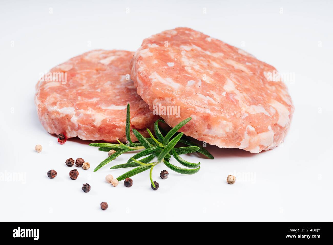 Raw chicken burger on a white plate in a rosemary branch and spices ...